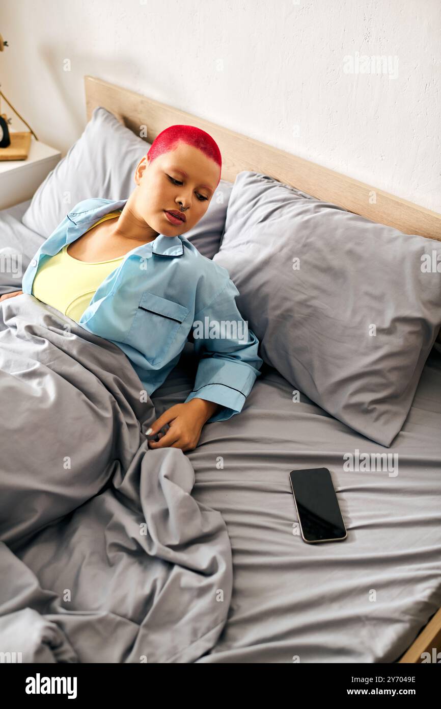A young woman with vibrant red hair lounges in her bed, reaching for ...