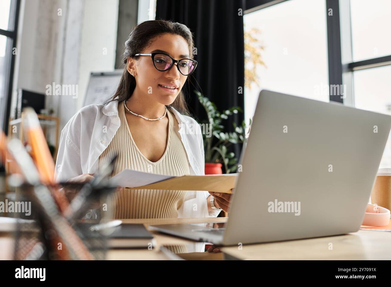 A young woman in glasses sits at her desk, reviewing documents while ...