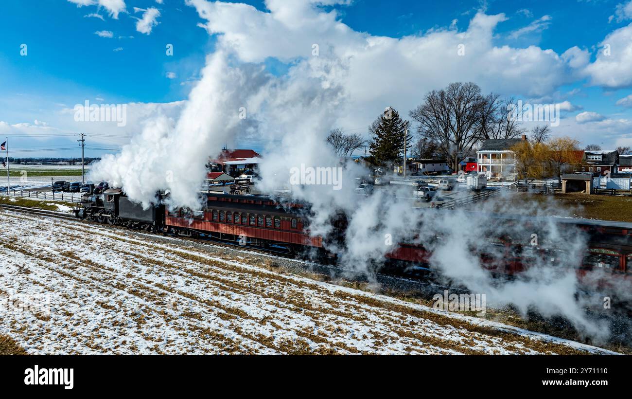 A vintage steam train moves through a landscape of snow-dusted fields ...