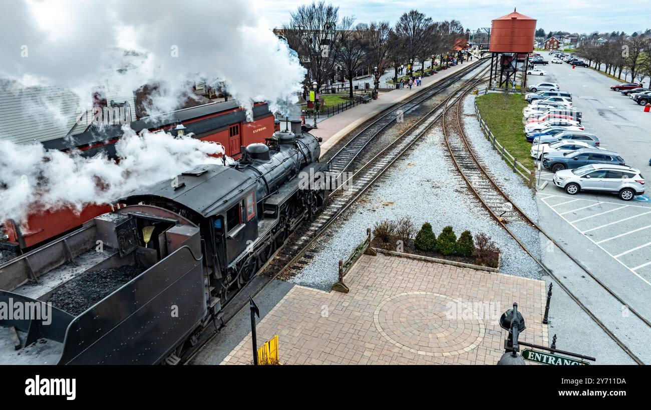 A steam locomotive puffs white smoke as it moves along railway tracks ...
