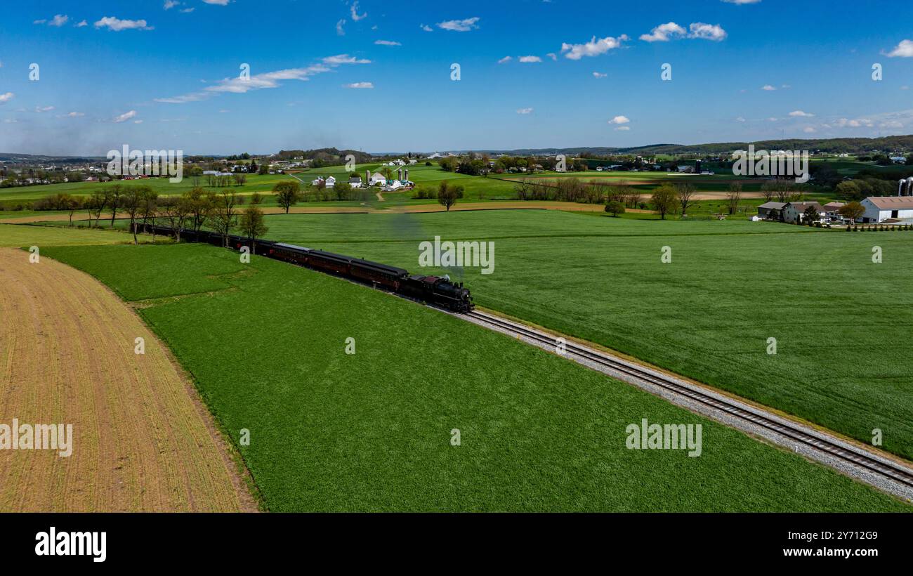 A vintage steam train winds its way through expansive green fields ...