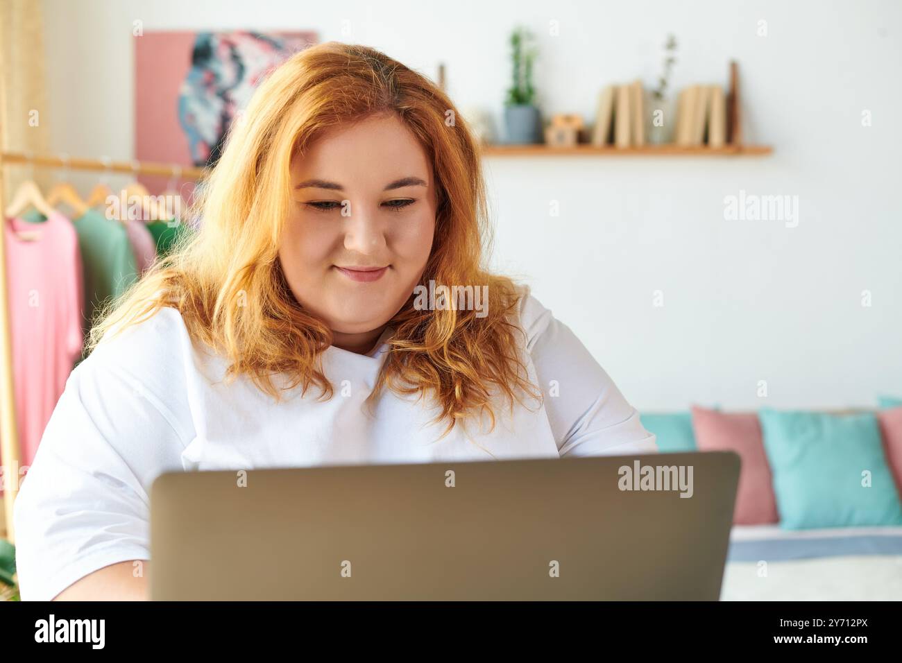 A beautiful plus size woman smiles as she types on her laptop, immersed ...