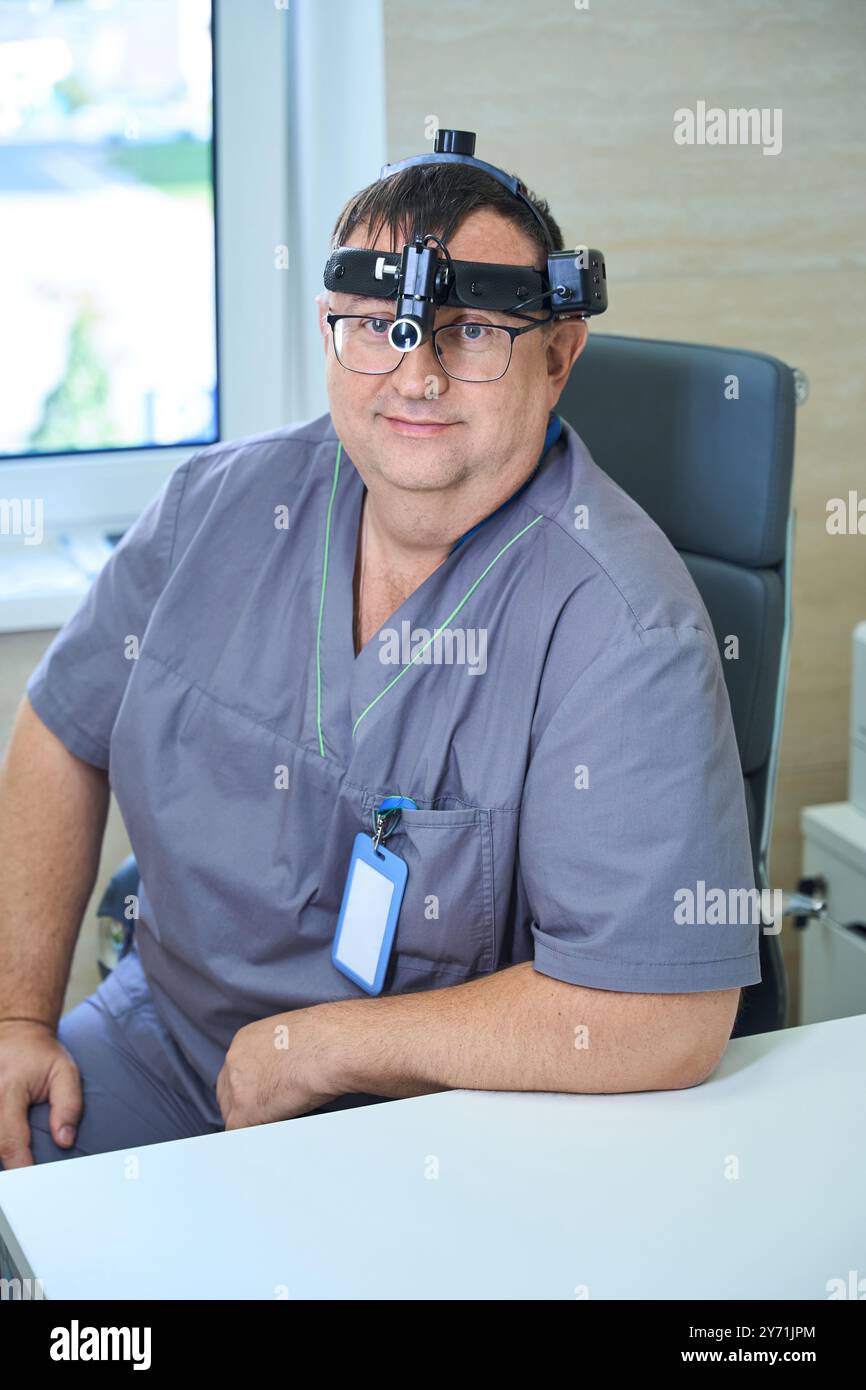Doctor in clinic with head mirror, seated Stock Photo - Alamy