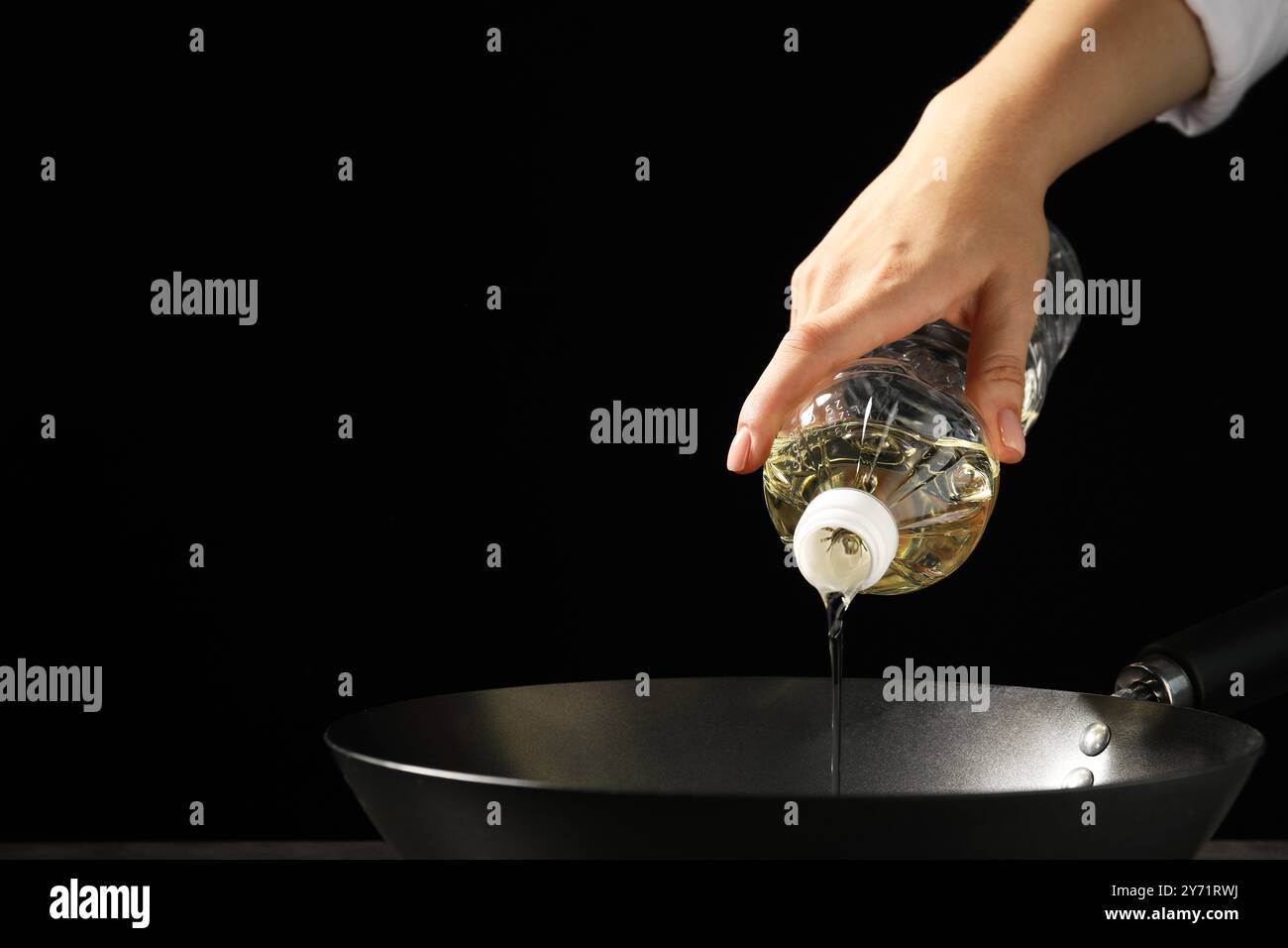 Woman pouring oil into frying pan at dark gray textured table against ...