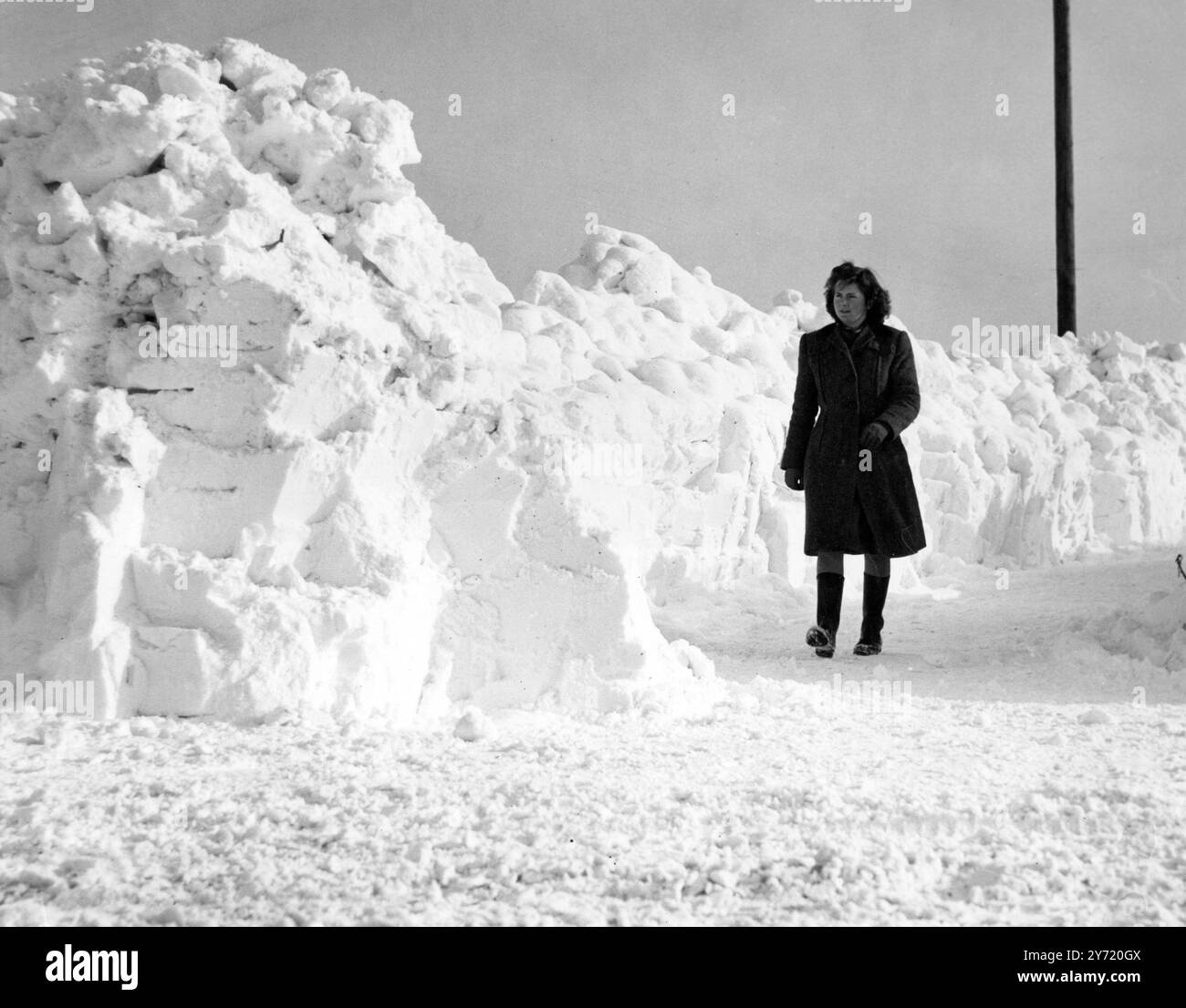 A lone woman walks along the road piled high with snow after being ...