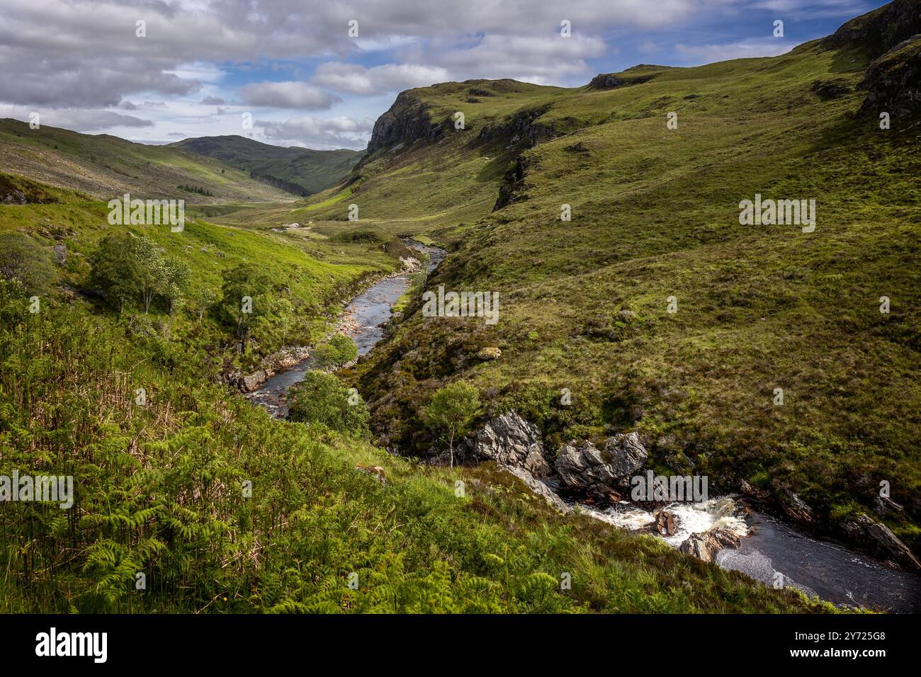 Typical Scottish landscape with hills, rocks, a cloudy blue sky and the ...
