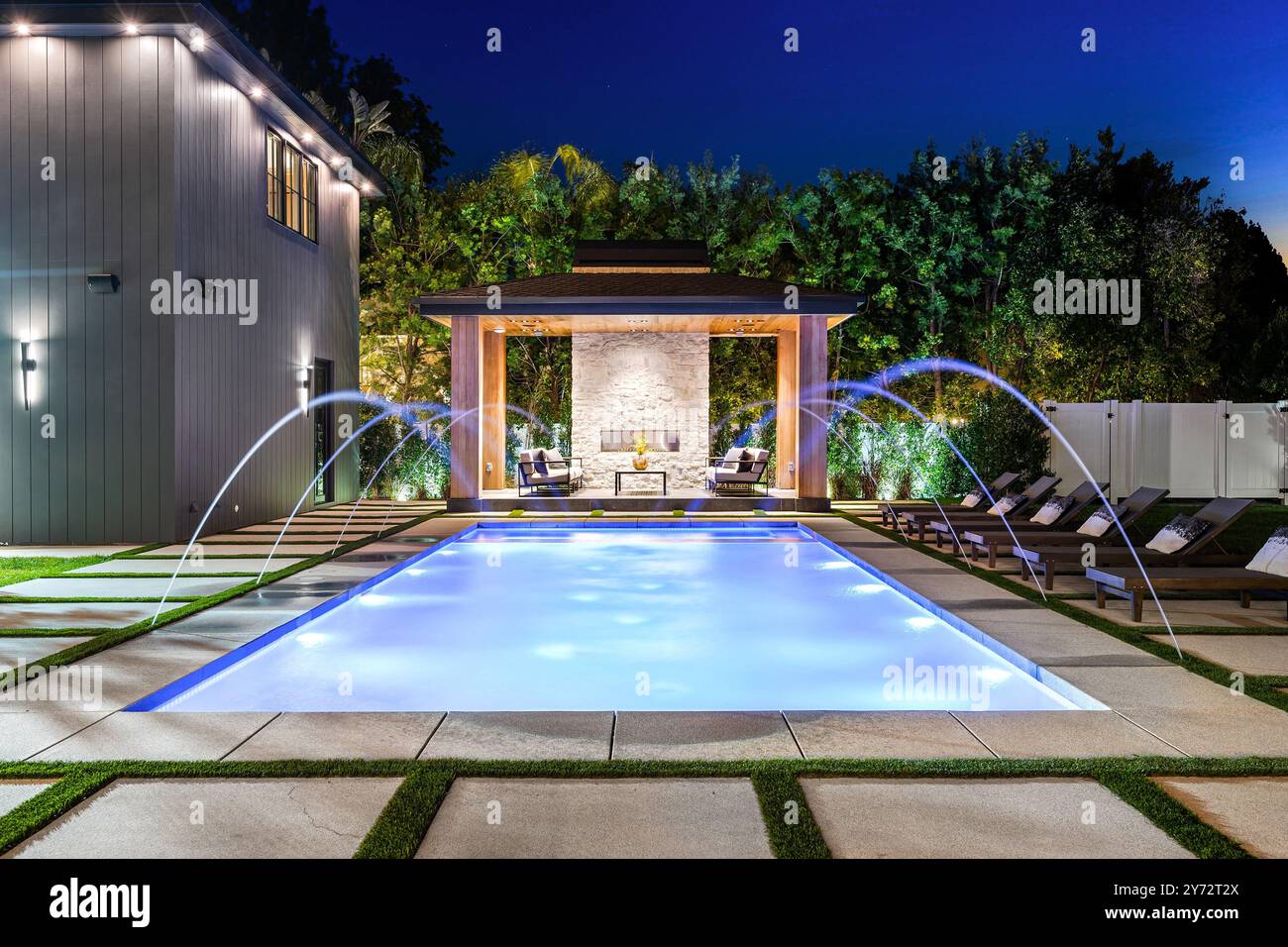 Luxurious modern backyard with illuminated swimming pool, lounge chairs ...