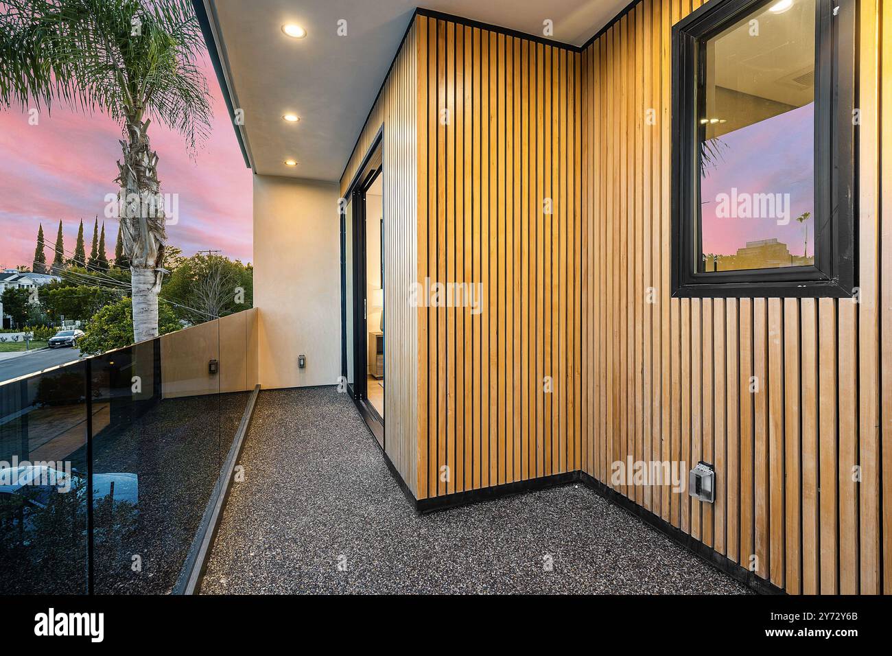 A modern balcony with wooden paneling, glass railings, and a sunset ...