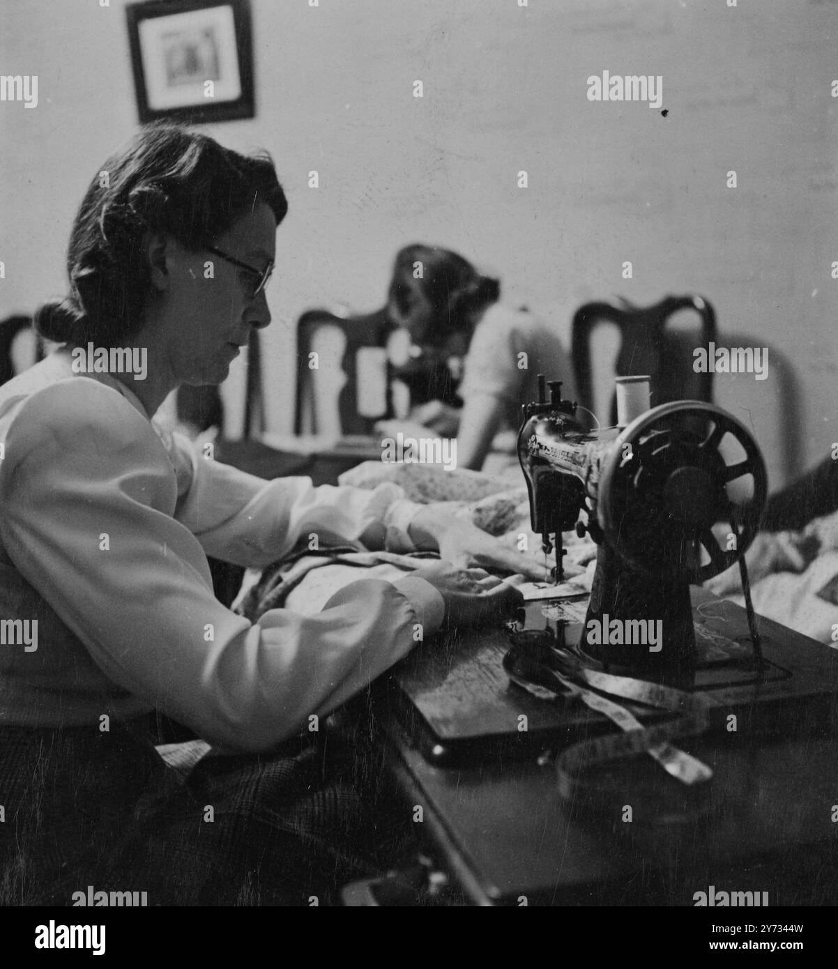Woman sewing using a sewing machine and young girl in background [no ...