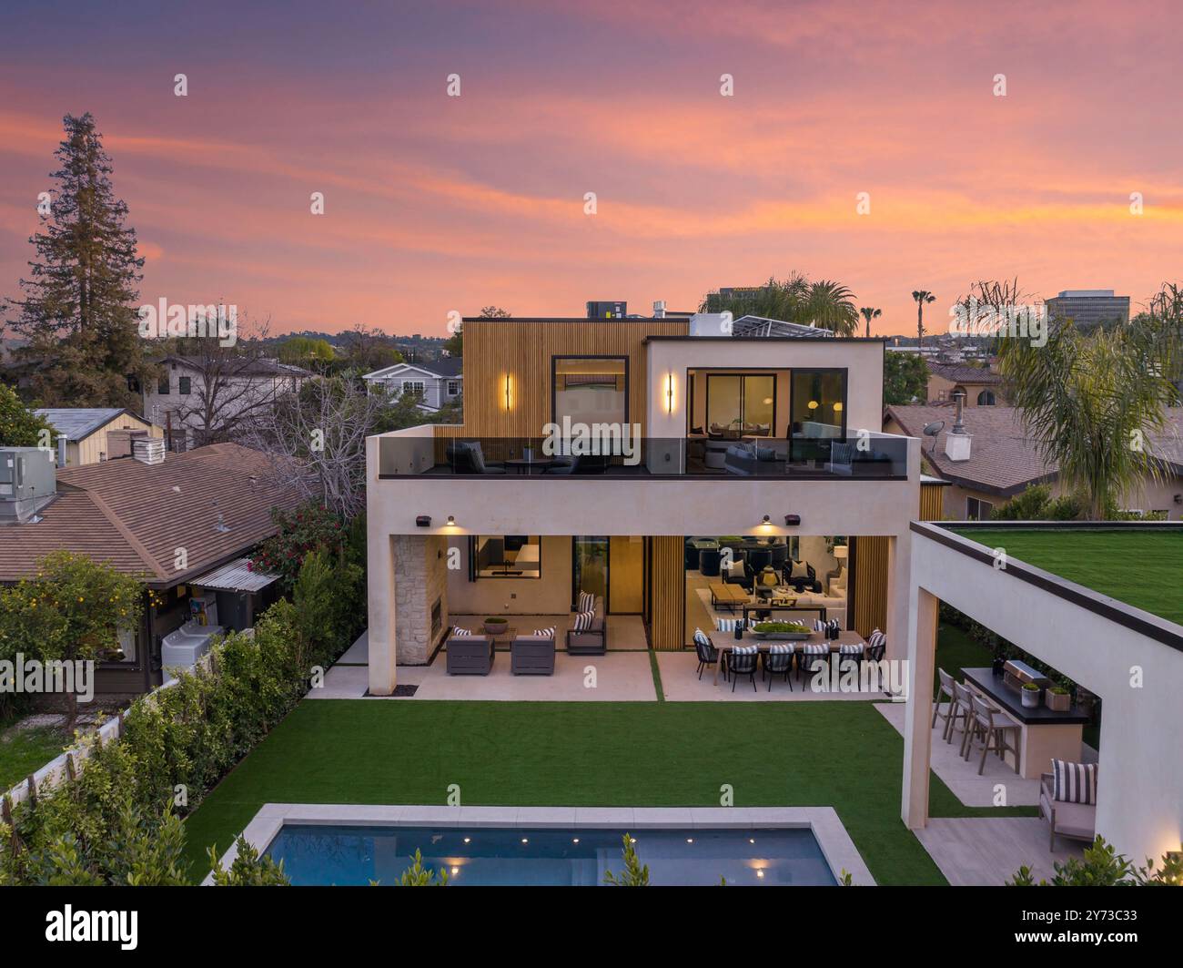 A modern two-story house with a pool and outdoor seating area at sunset ...