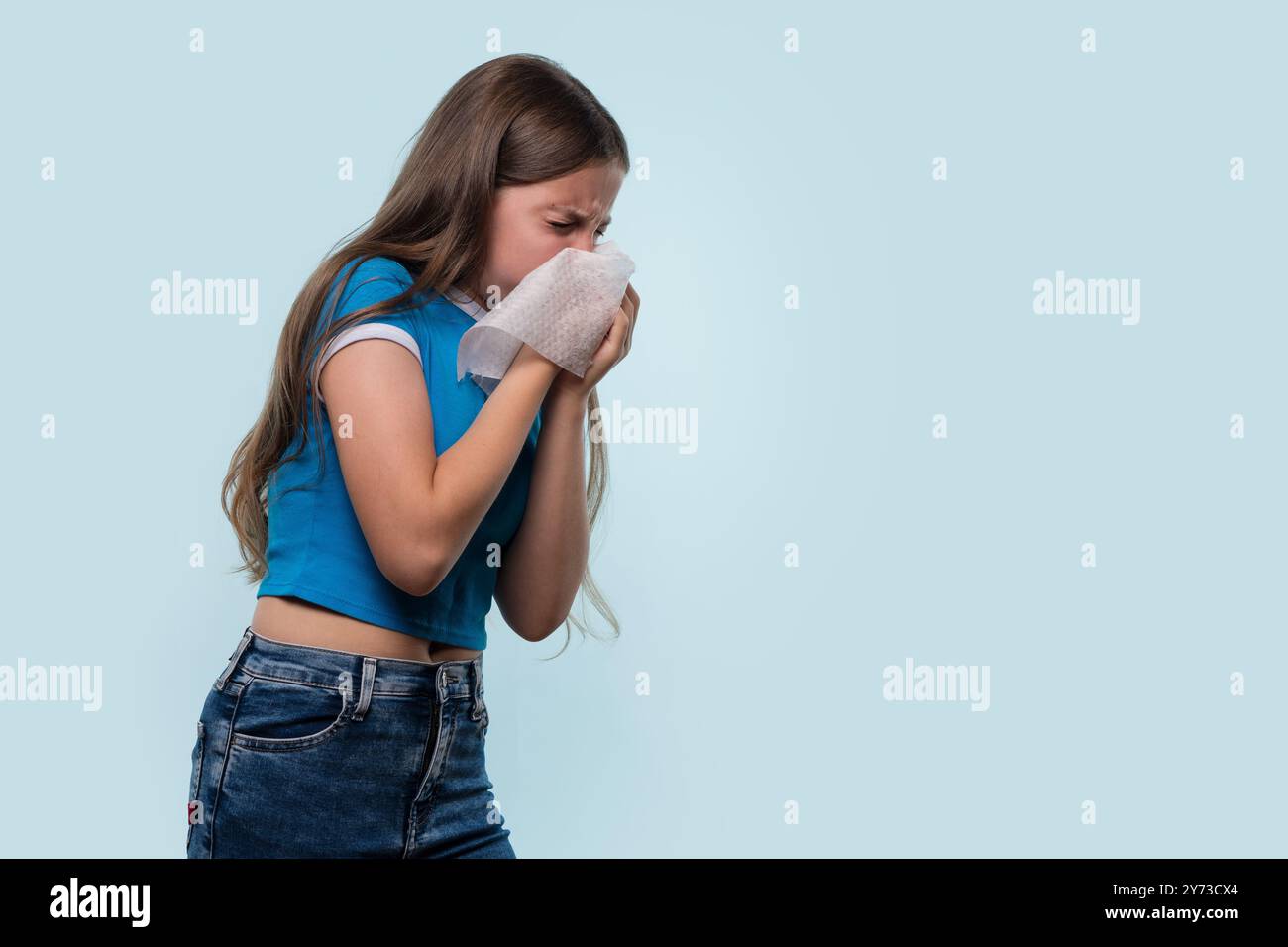 A young girl sneezing into a tissue, experiencing cold or allergy ...