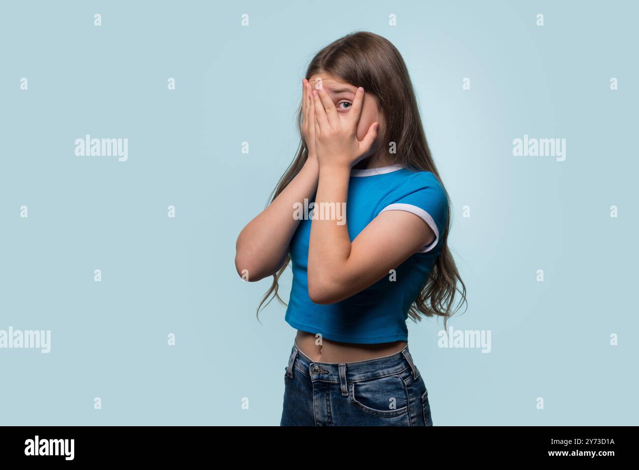 A young girl covering her face with her hands in embarrassment or fear ...