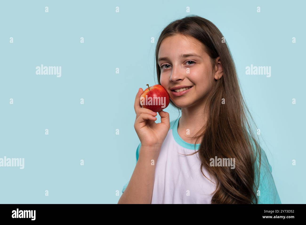 A young girl smiles while holding a red apple against her cheek ...