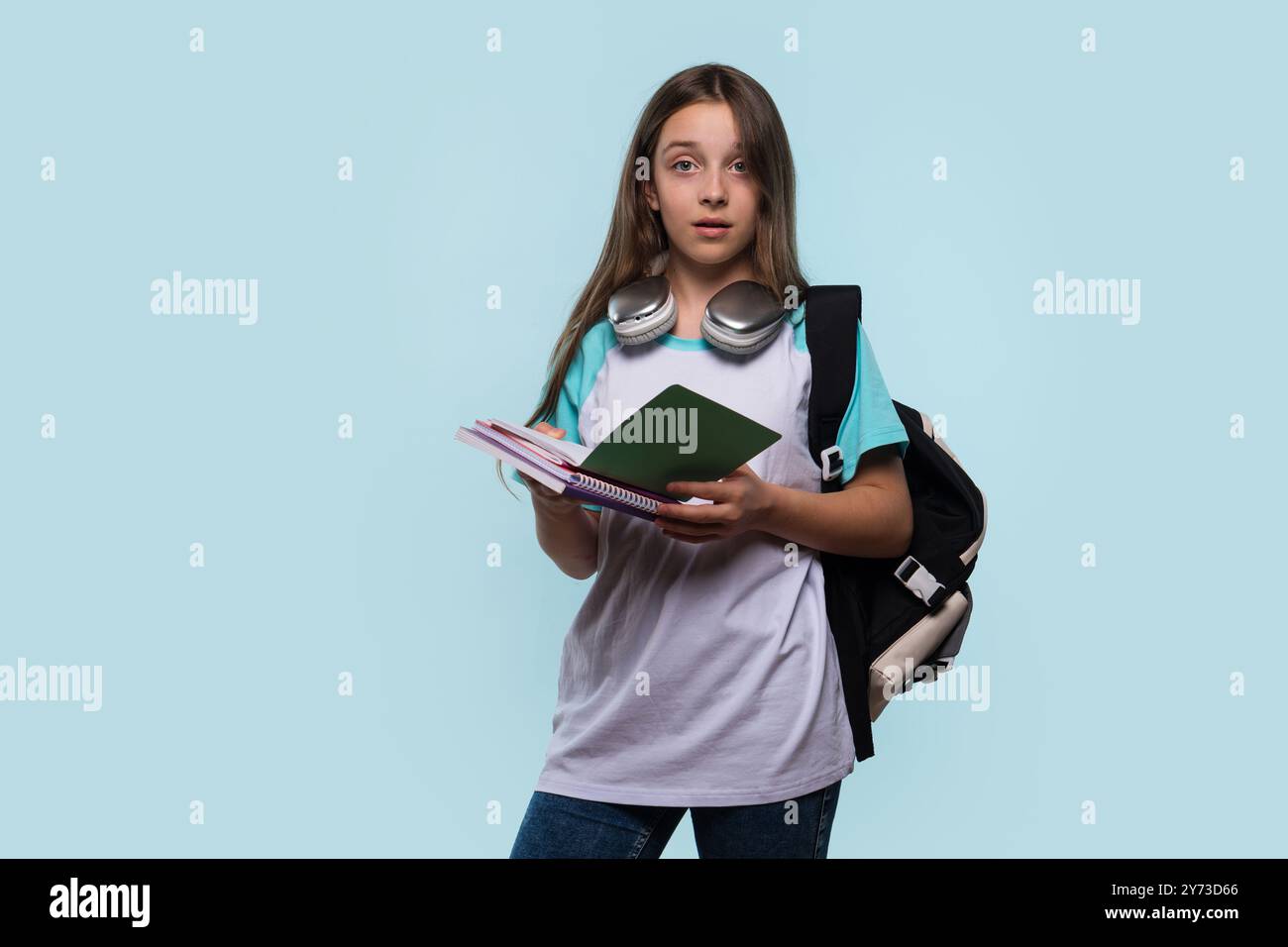 Surprised girl holding a notebook, wearing a backpack and headphones ...