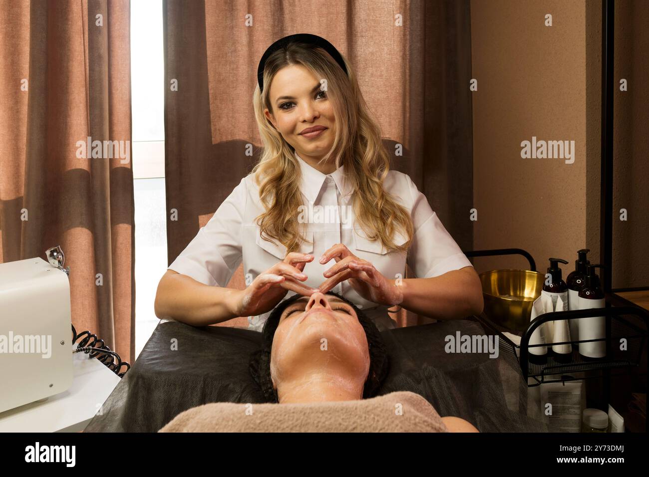 Aesthetician performing facial massage using cream on a relaxed client ...