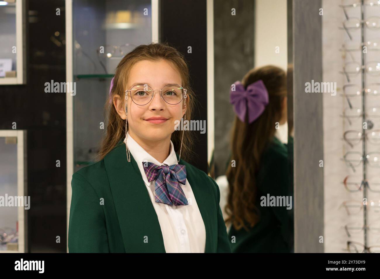 Girl in a school uniform standing inside an optical shop, smiling ...