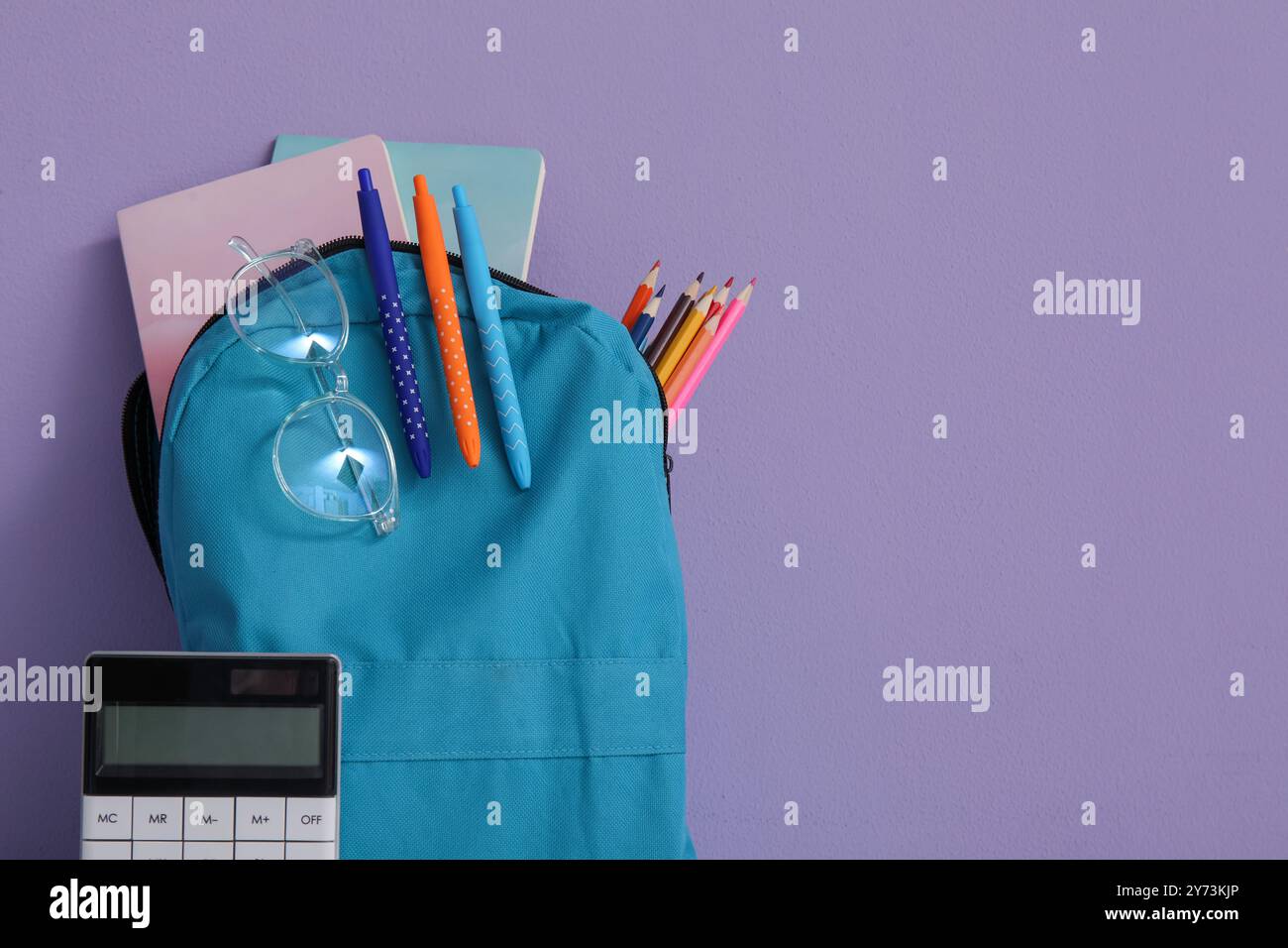 Blue school backpack with different stationery and calculator on purple ...
