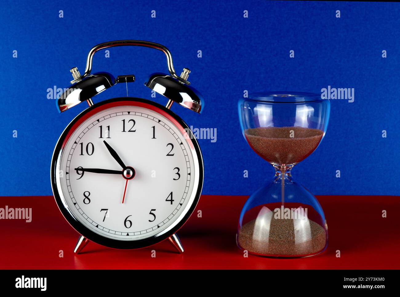 Hourglass and traditional alarm clock closeup view on a red base and ...