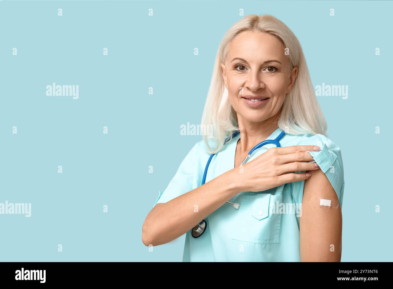 Mature female doctor with medical patch on arm against blue background ...