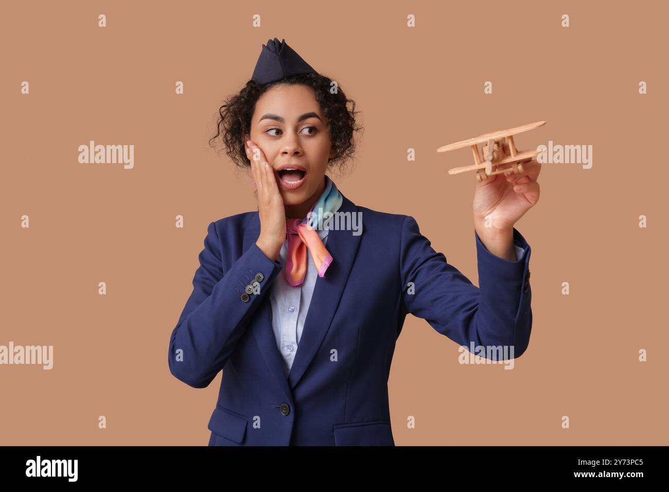 Surprised African-American stewardess with toy plane on beige ...