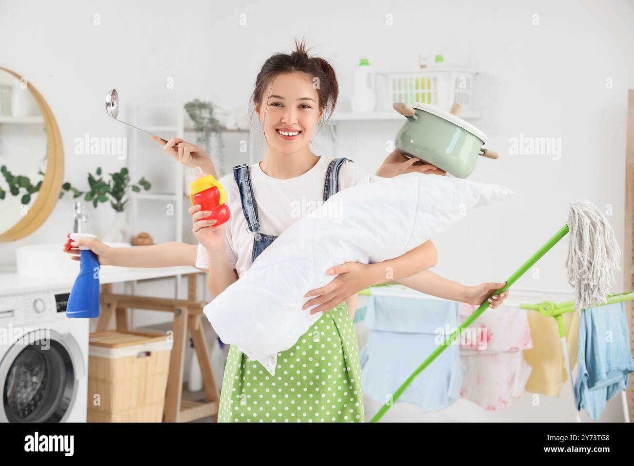 Overwhelmed Asian mother with baby, bottle of milk, kitchen utensils ...