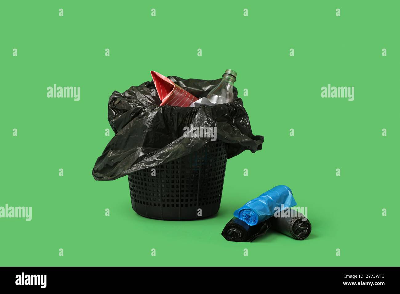 Full trash bin and rolls of garbage bags on green background Stock ...