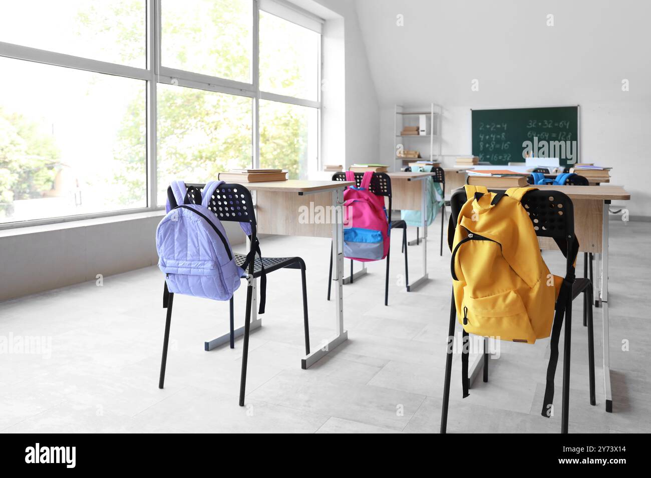 Interior of empty classroom with desks, backpacks on chairs and ...