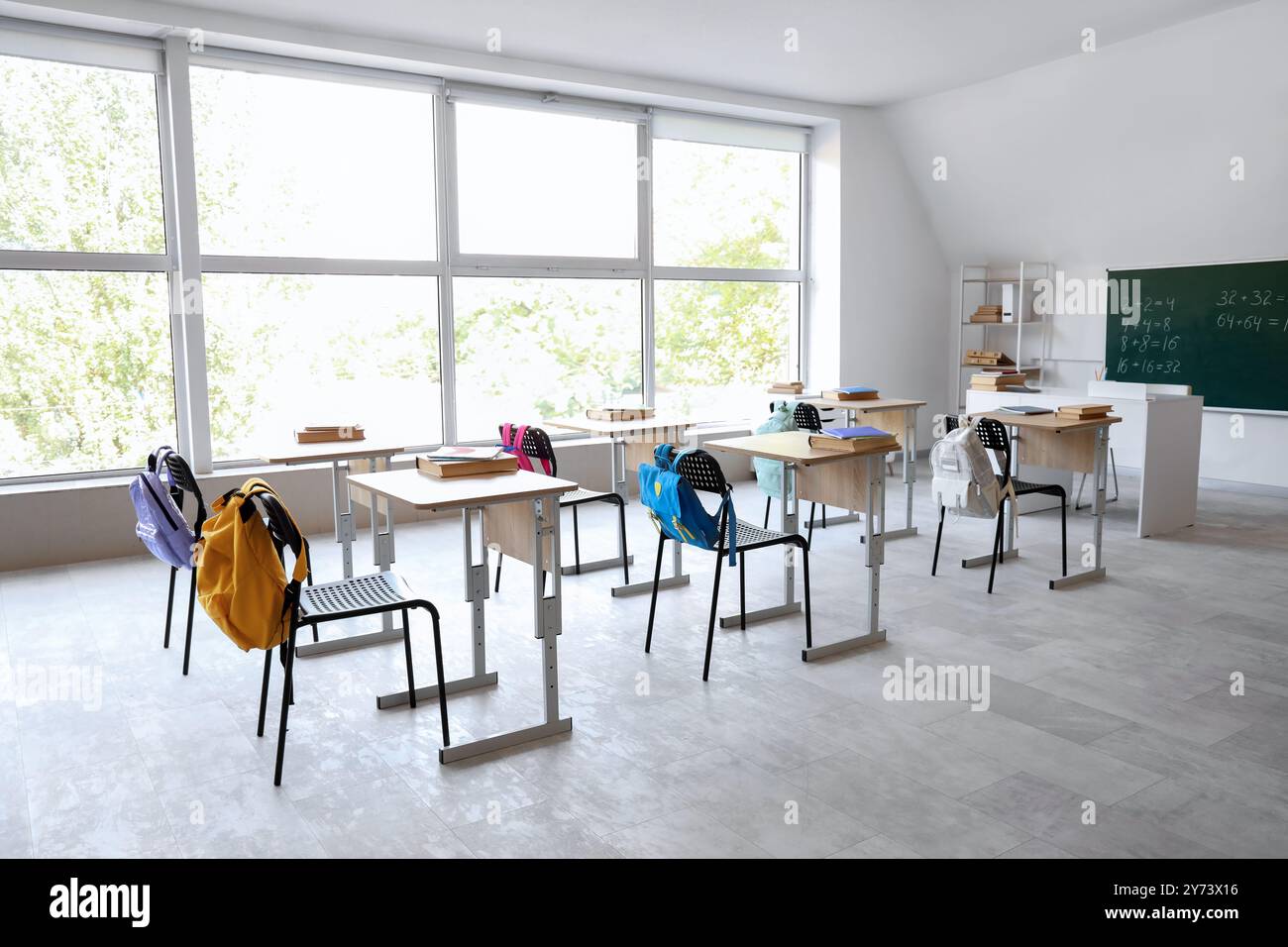 Interior of empty classroom with desks, backpacks on chairs and ...