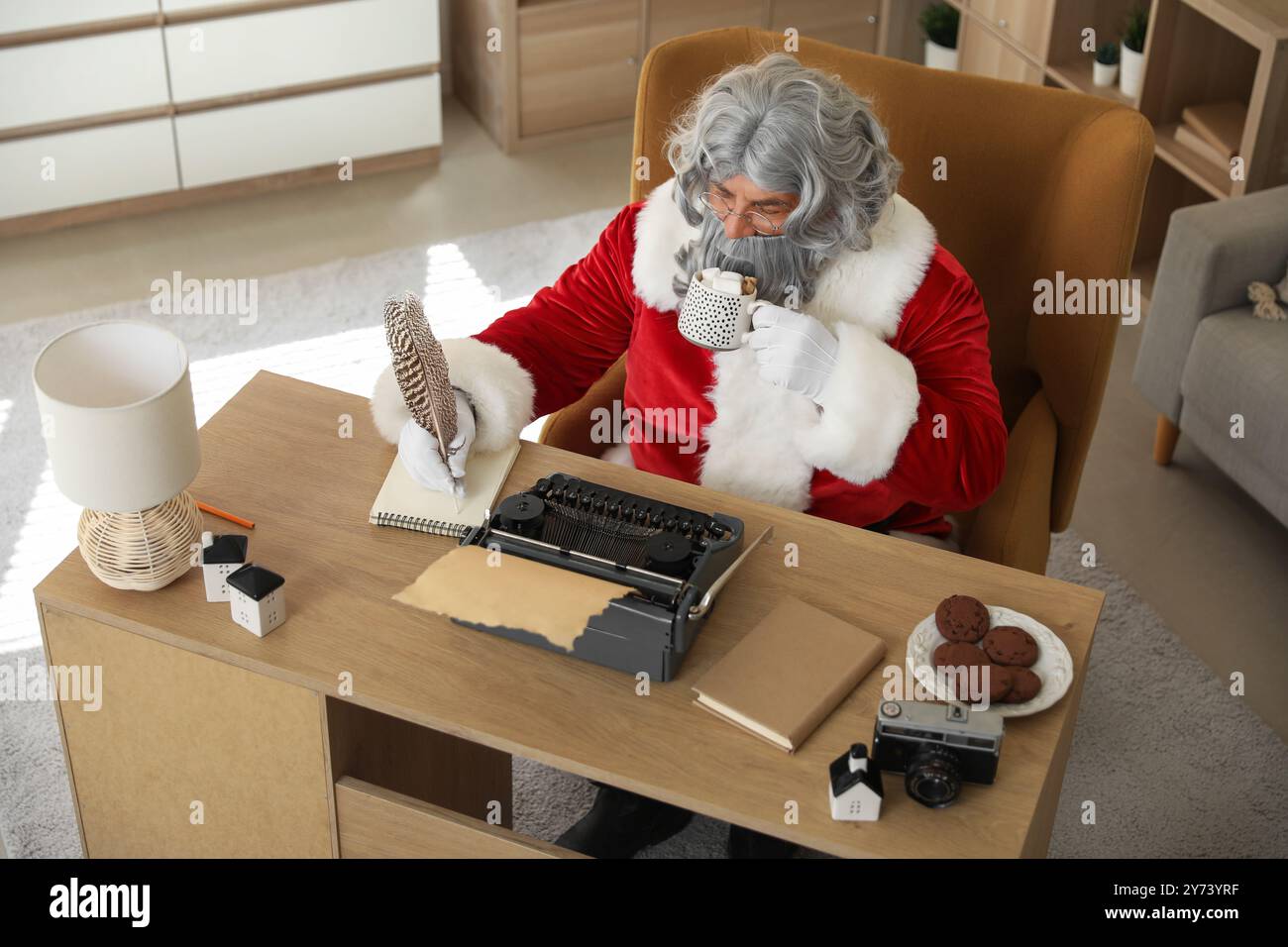 Santa Claus with typewriter, feather and cup of cocoa taking notes ...