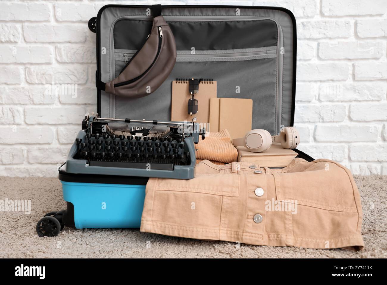 Open suitcase with vintage typewriter and clothes on carpet near white ...