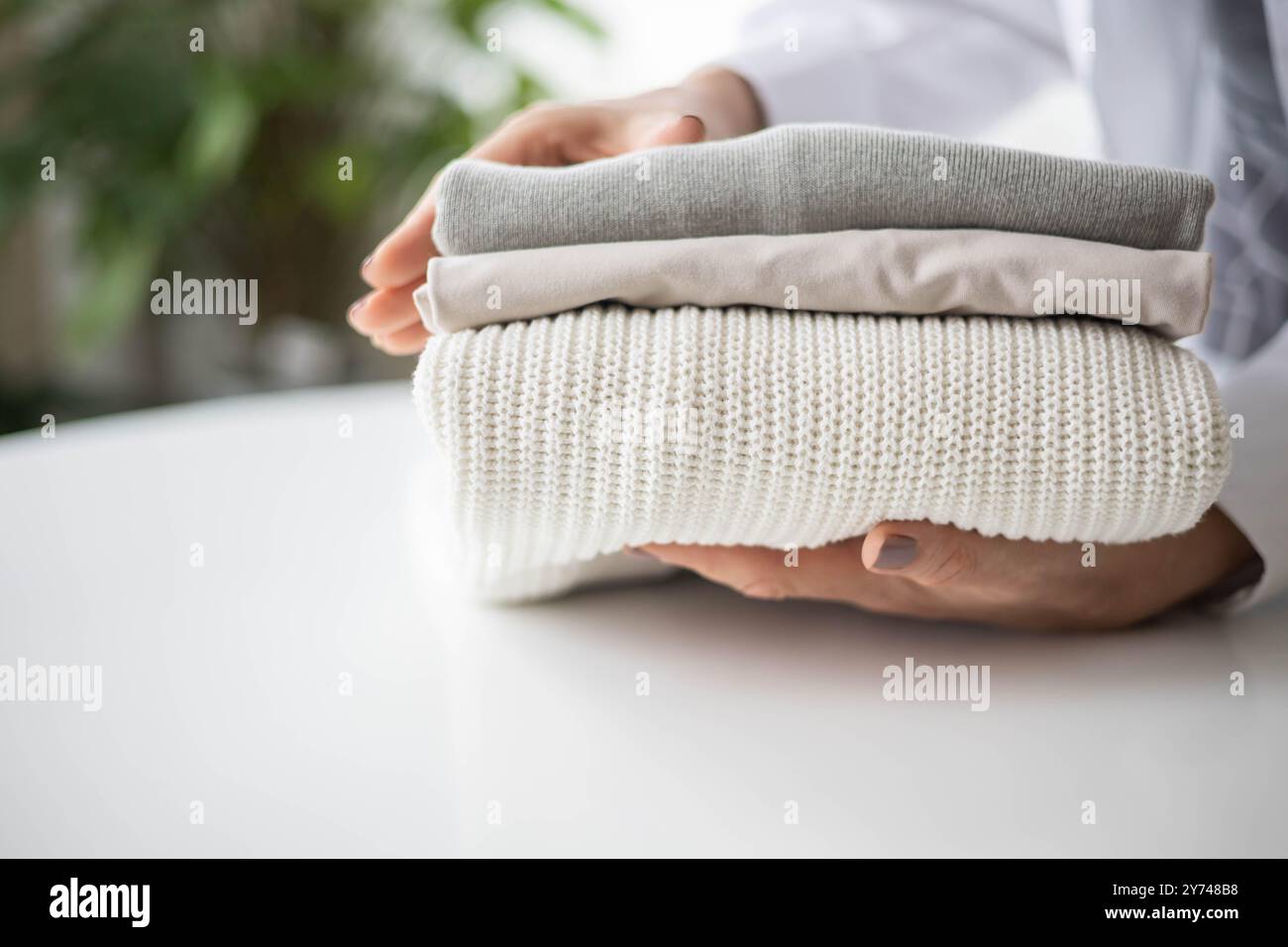 Women's hands hold a stack of neat, clean, cotton clothes in neutral ...