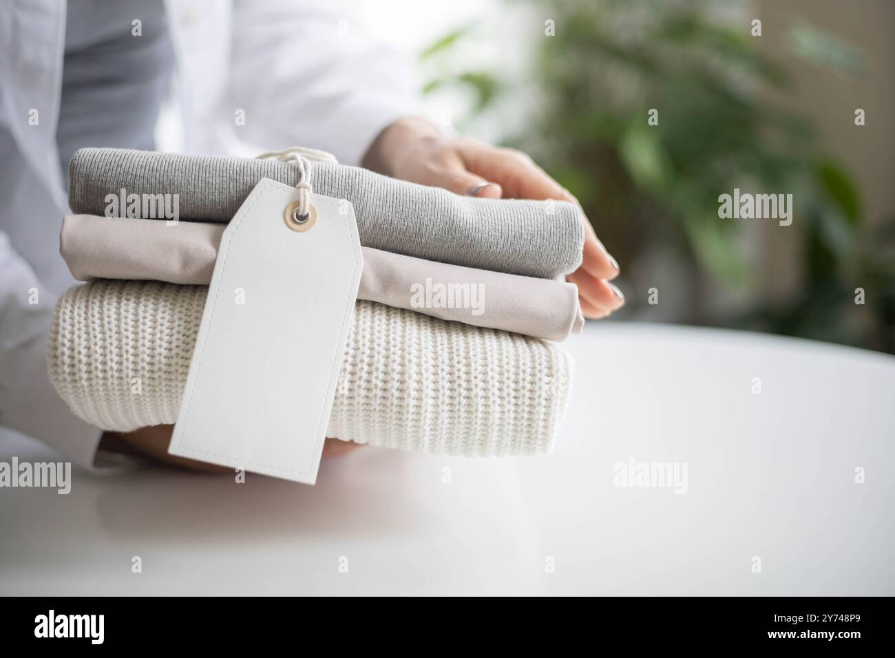 Women's hands hold a stack of neat, clean, cotton clothes in neutral ...