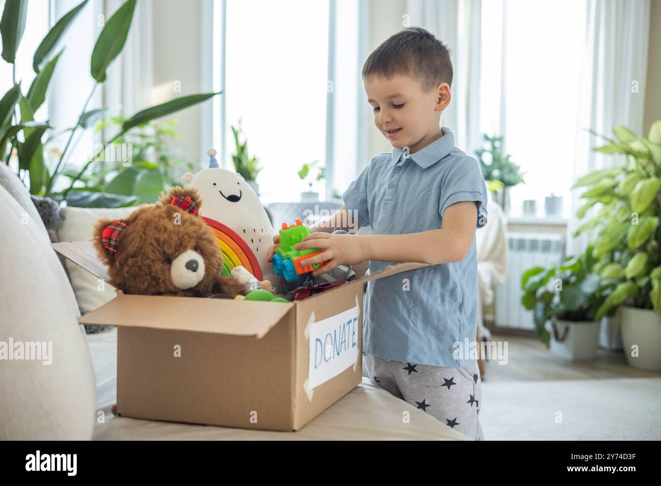 Boy child puts toys in a cardboard box for charity. Donation concept ...