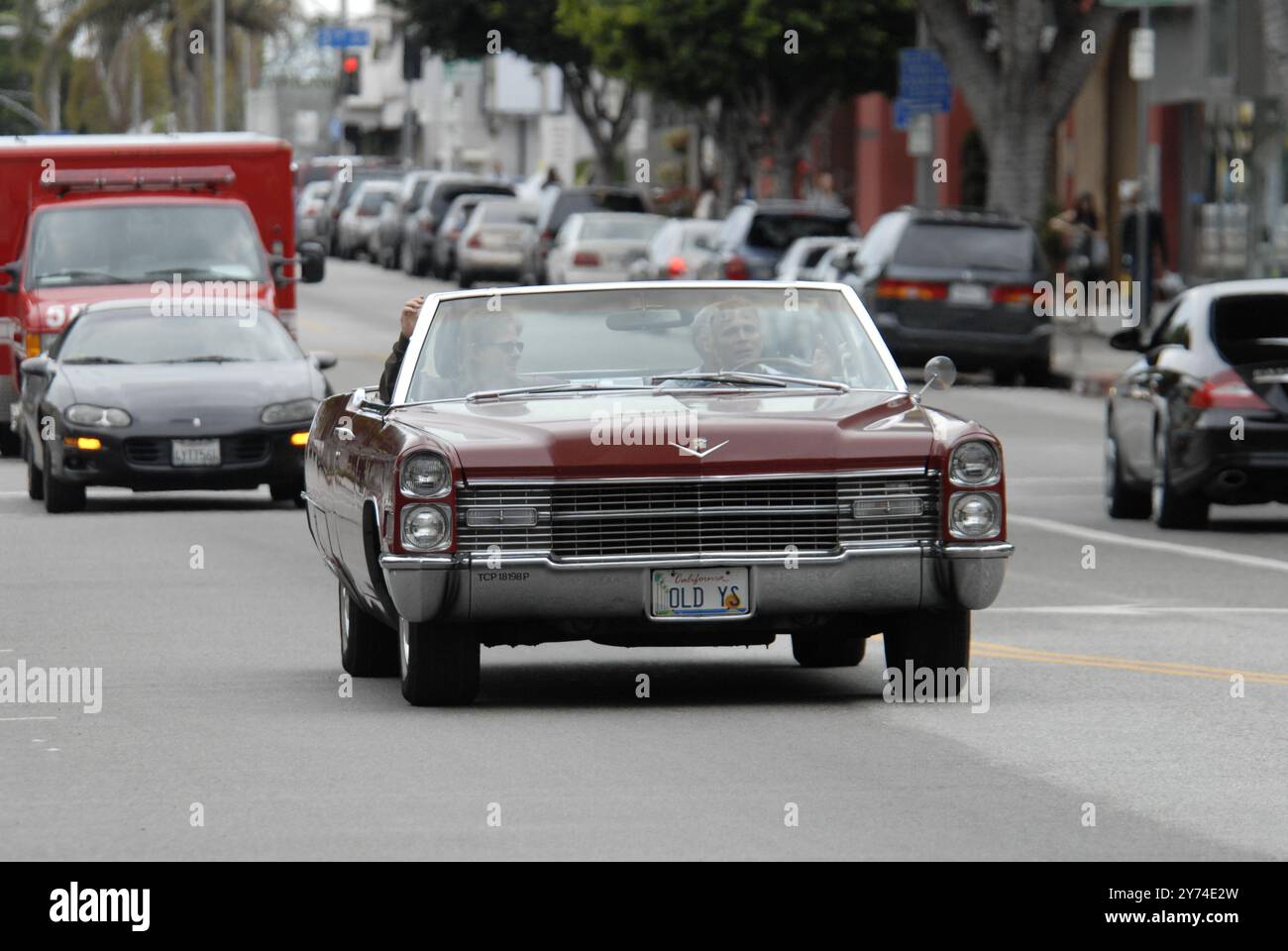 A classic red Cadillac convertible rolls down a city street with ...