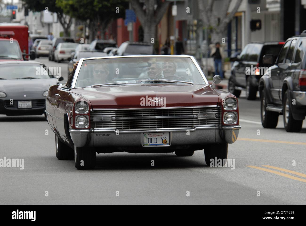 A classic red Cadillac convertible rolls down a city street with ...