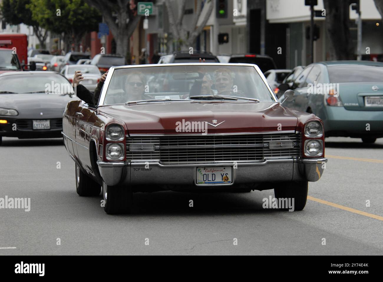 A classic red Cadillac convertible rolls down a city street with ...