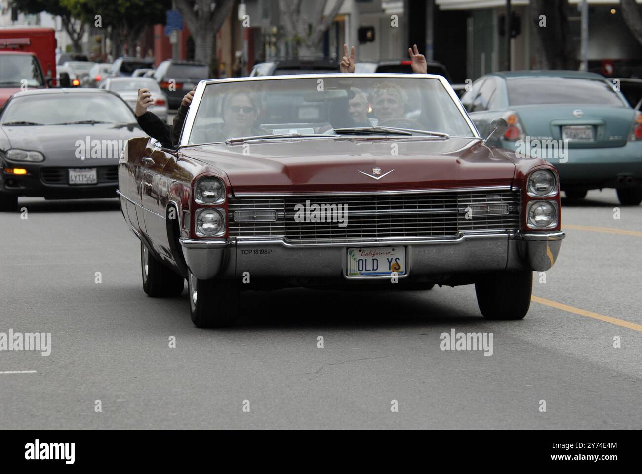 A classic red Cadillac convertible rolls down a city street with ...
