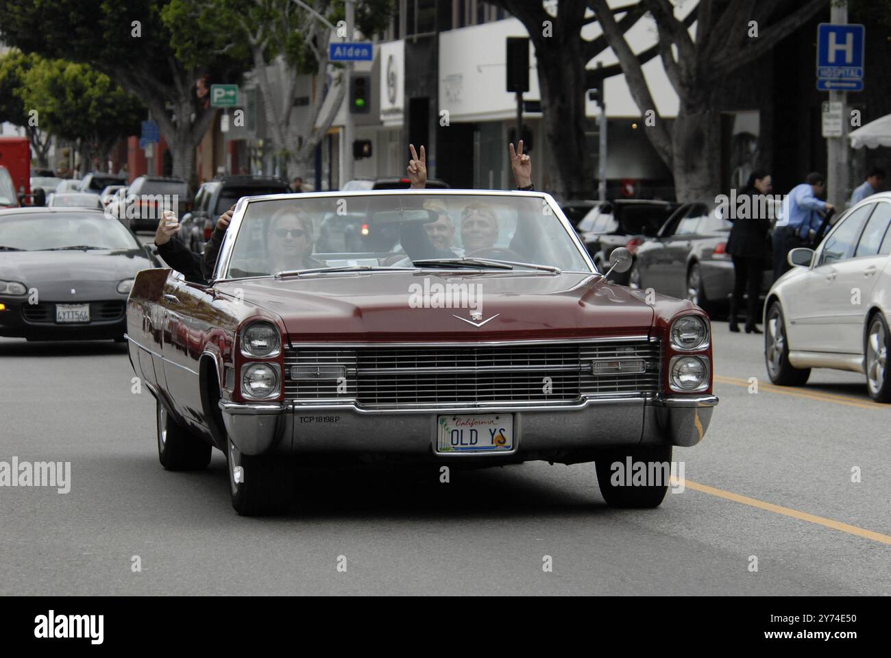 A classic red Cadillac convertible rolls down a city street with ...