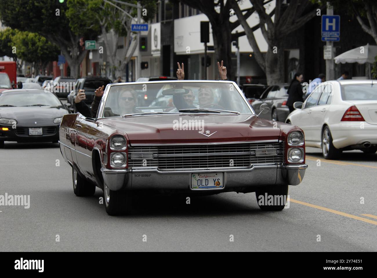 A classic red Cadillac convertible rolls down a city street with ...