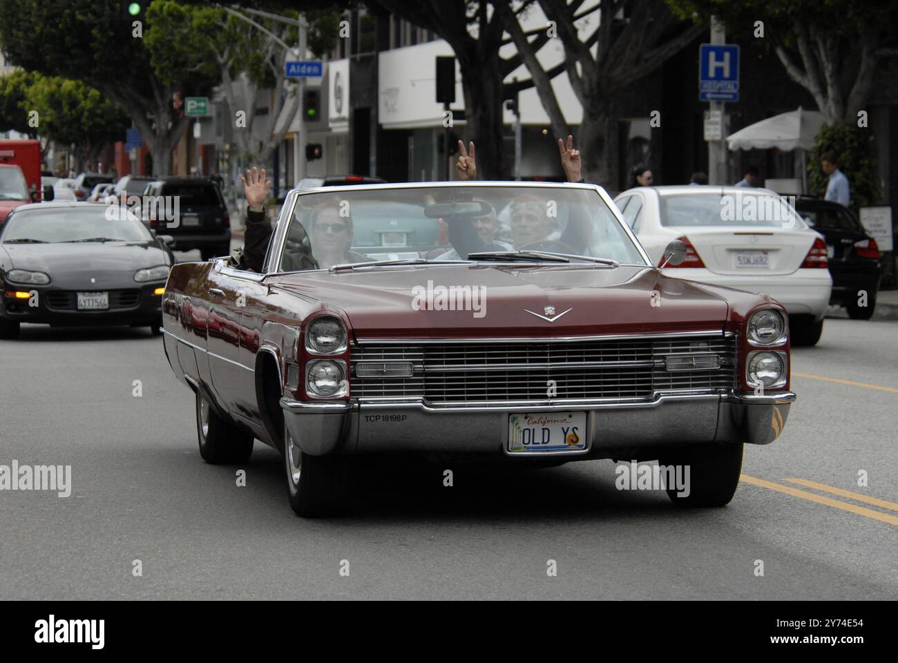 A classic red Cadillac convertible rolls down a city street with ...
