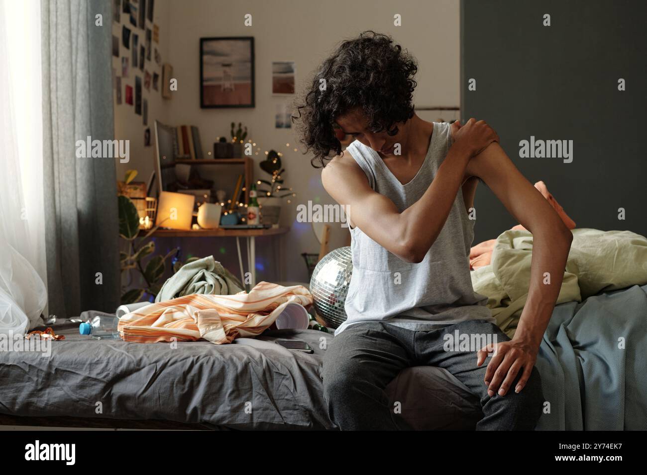 Young man with headache and other symptoms of hangover sitting on bed ...