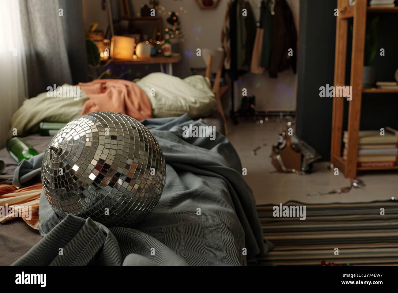 Glittering disco ball lying on creased bed with grey blanket, attire ...