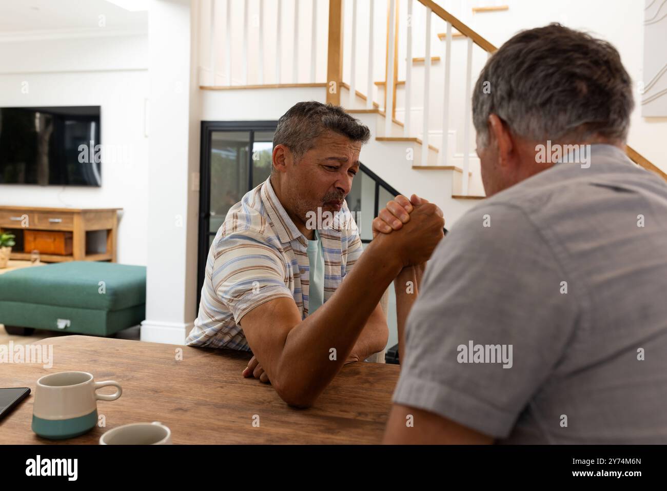 Arm wrestling, two senior diverse friends competing at table in living ...