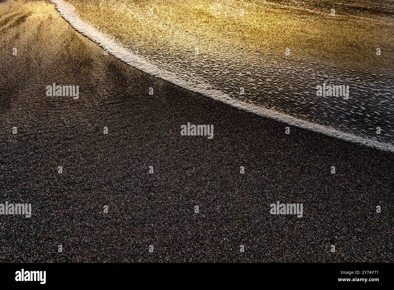 Waves on a sandy beach forming beautiful colored patterns in the glow ...