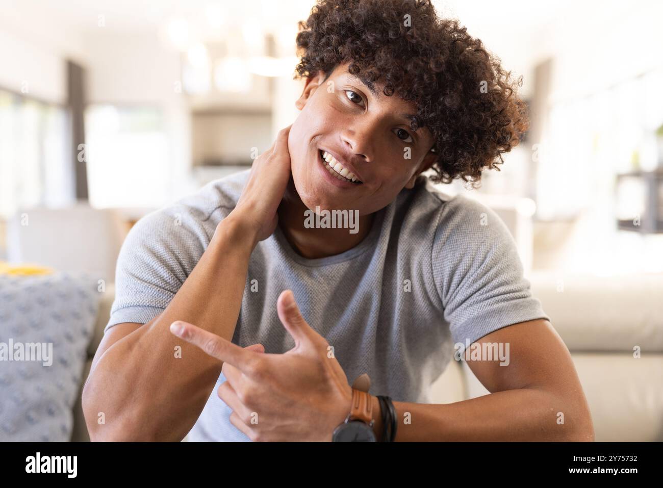 On video call, Smiling man pointing and touching neck while relaxing at ...