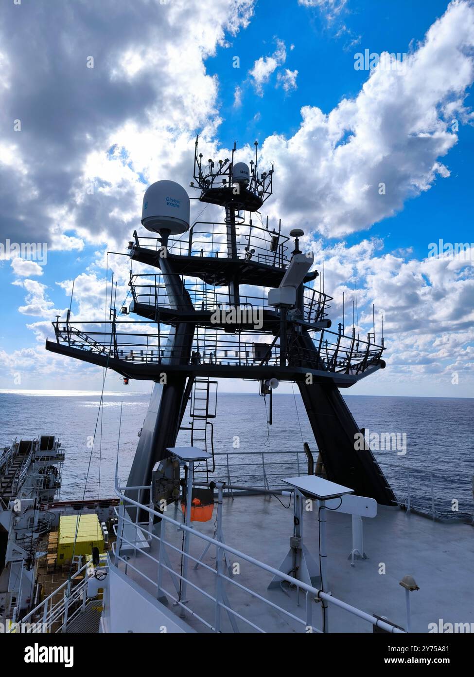 A view of a ship's radar tower against a bright blue sky with scattered ...