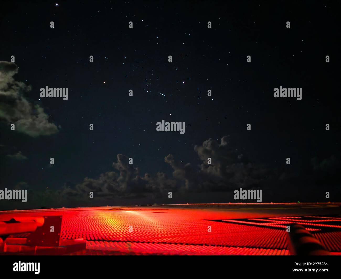 A night sky filled with stars above a red-lit surface with scattered ...