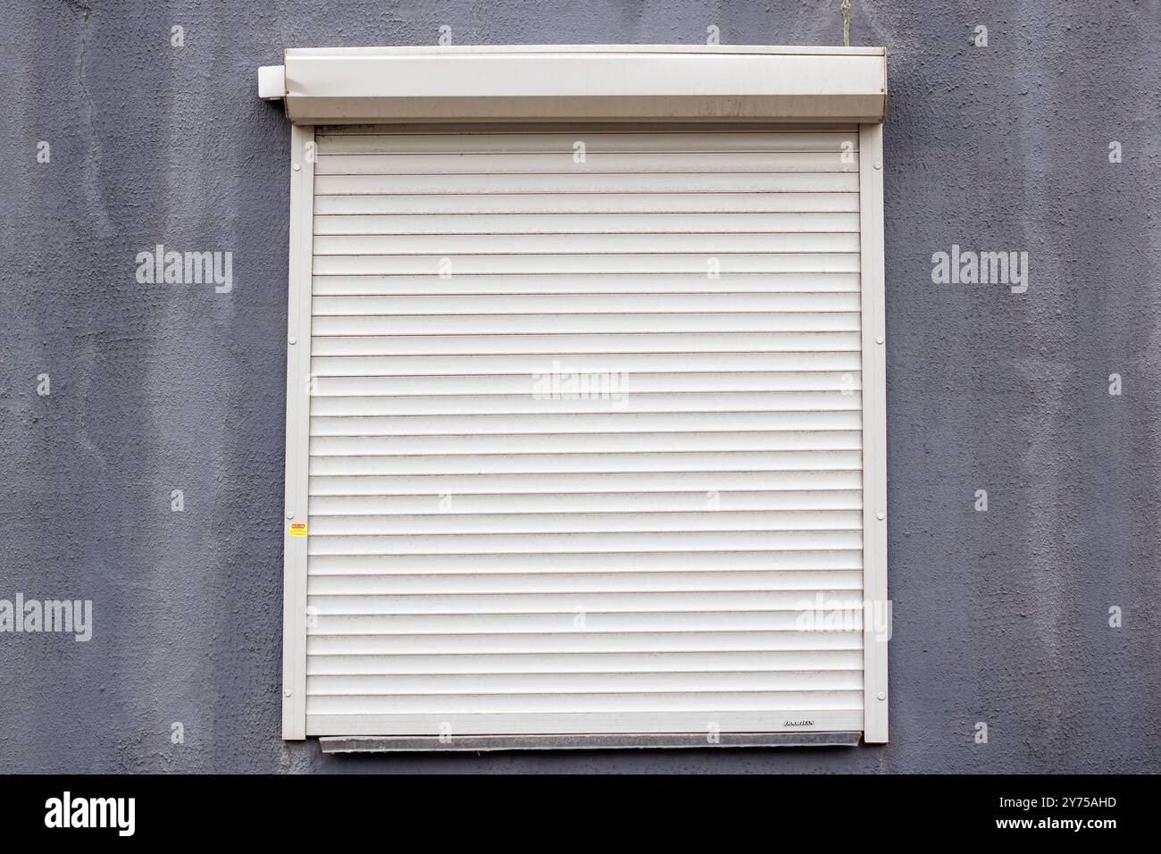 A white roller shutter is currently positioned on a gray wall, creating ...