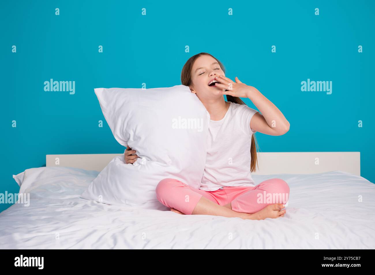 Full body photo of cute little girl hug pillow yawn sit bed sleeping ...