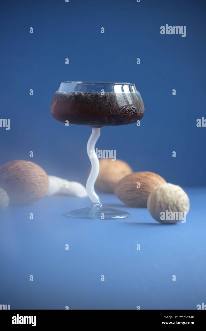 A chic burgundy cocktail, served in a glass with a white wavy stem ...